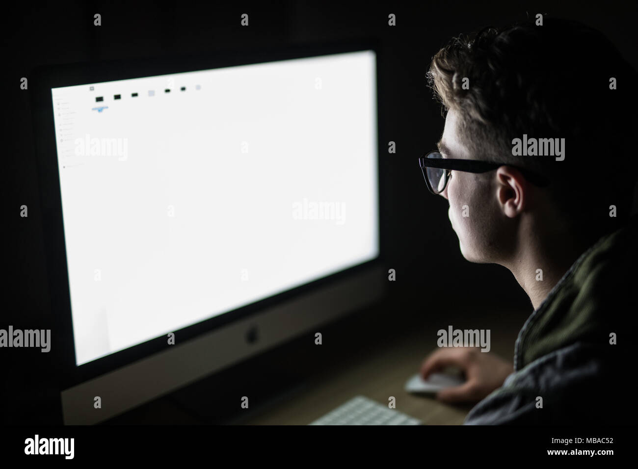Closeup of young man sitting and using blank screen computer in dark ...