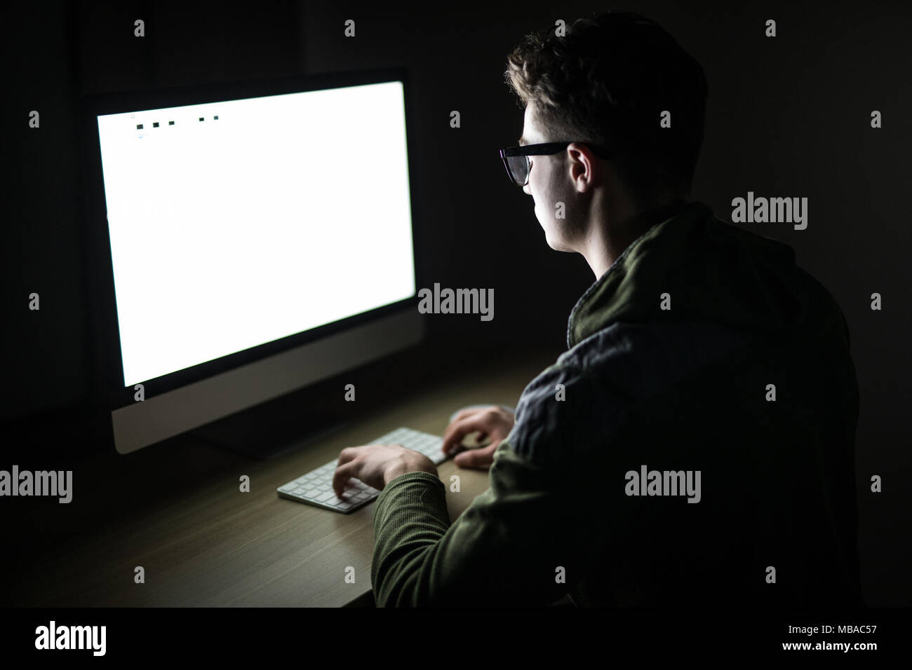 Closeup of young man sitting and using blank screen computer in dark ...