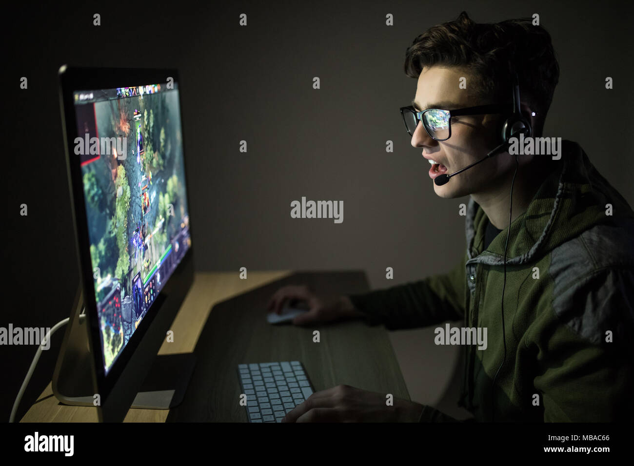 night play. young gamer in headphones and glasses using computer for ...