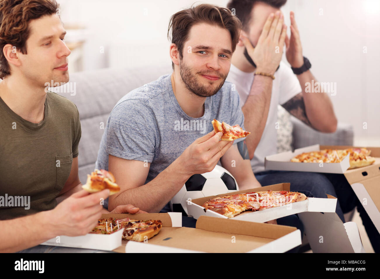 Happy male friends eating pizza and watching tv Stock Photo - Alamy