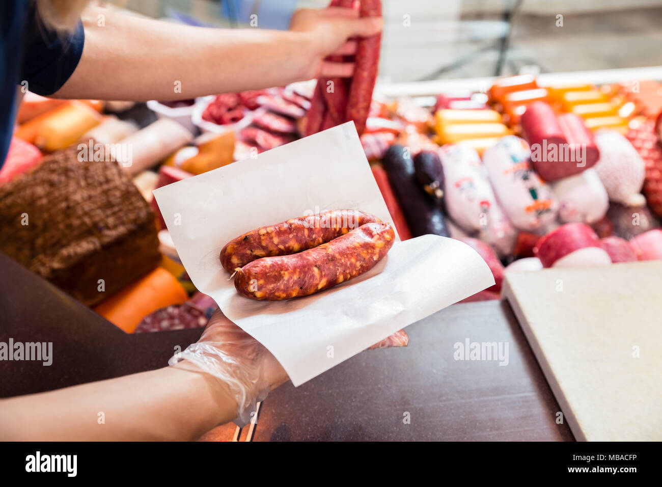 Sales woman in butchery holding sausage wrapped in paper Stock Photo ...