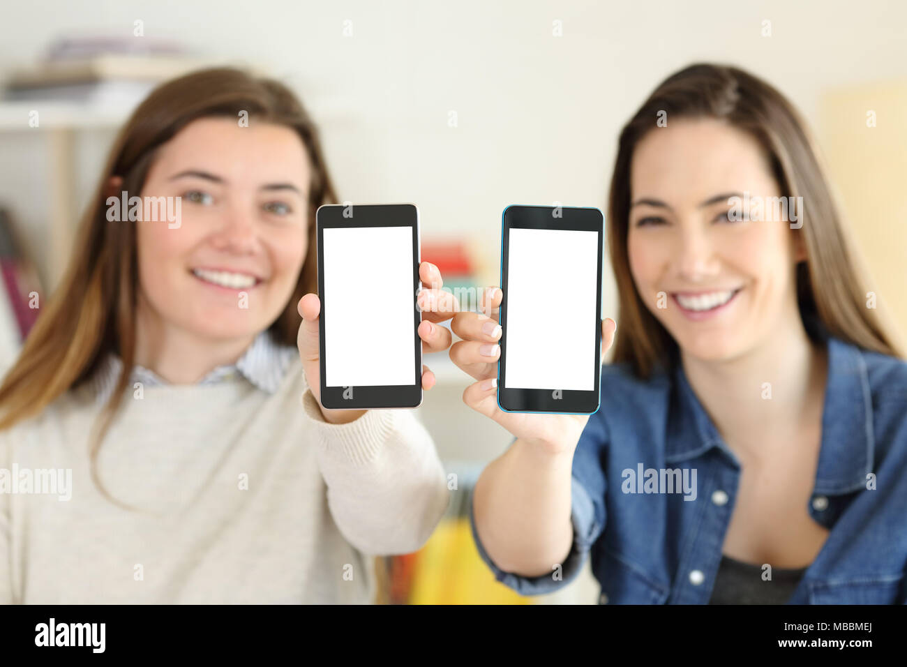 Two happy students showing their both smart phone screens to camera at ...