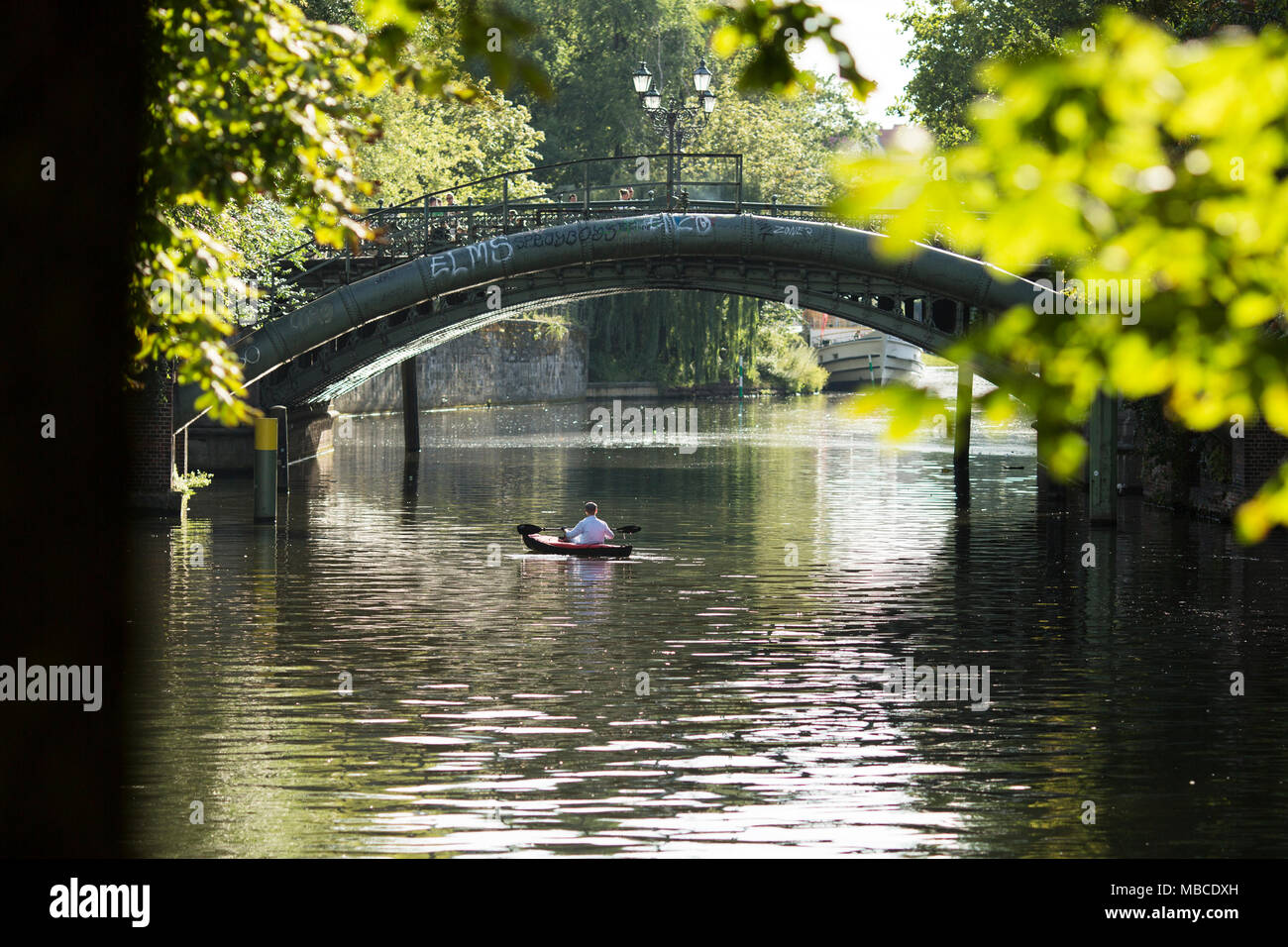 A man paddling a kayak under a bridge along the Landwehr Canal in the ...