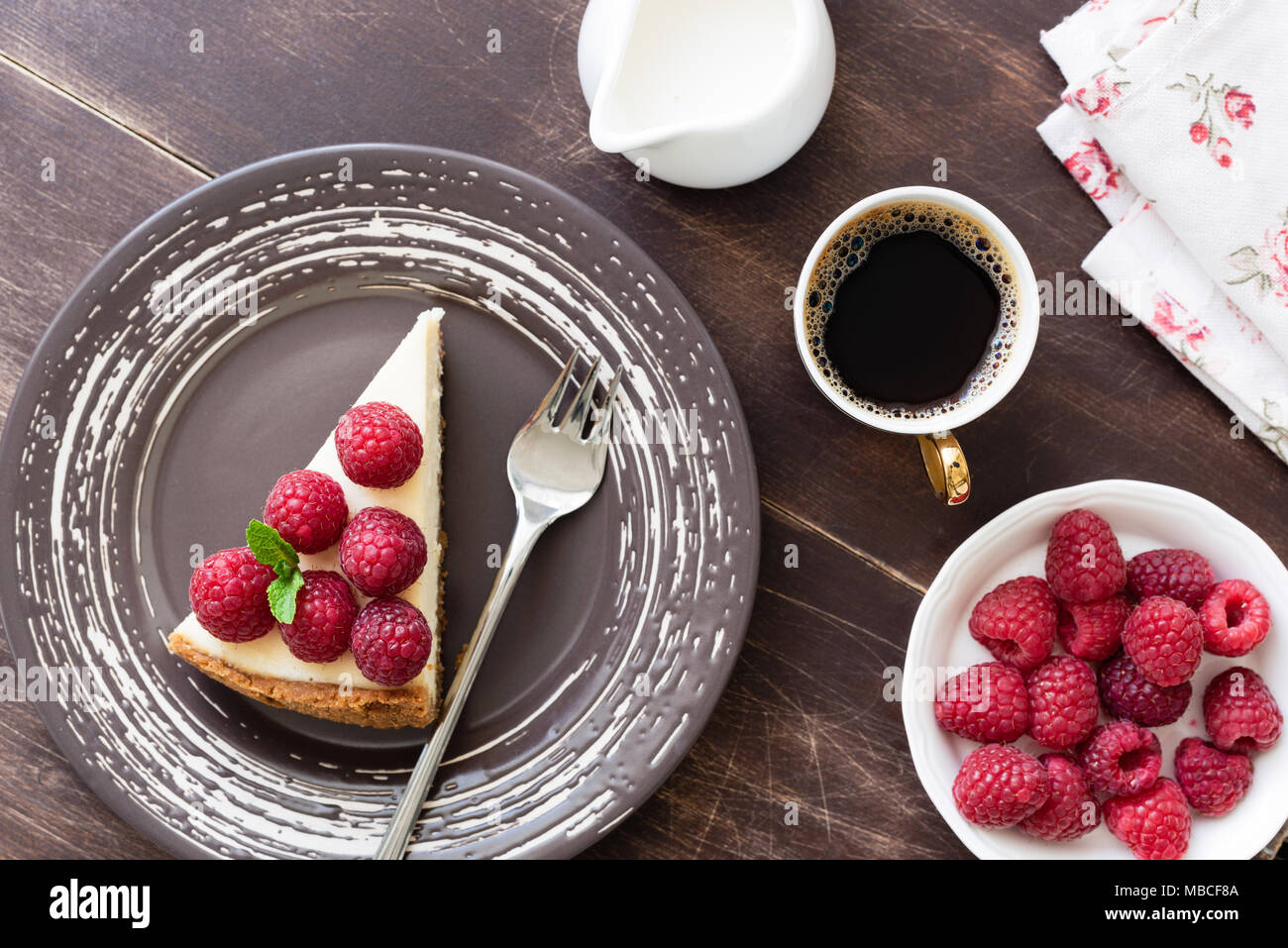 Slice of cheesecake with raspberries and cup of coffee on wood table ...
