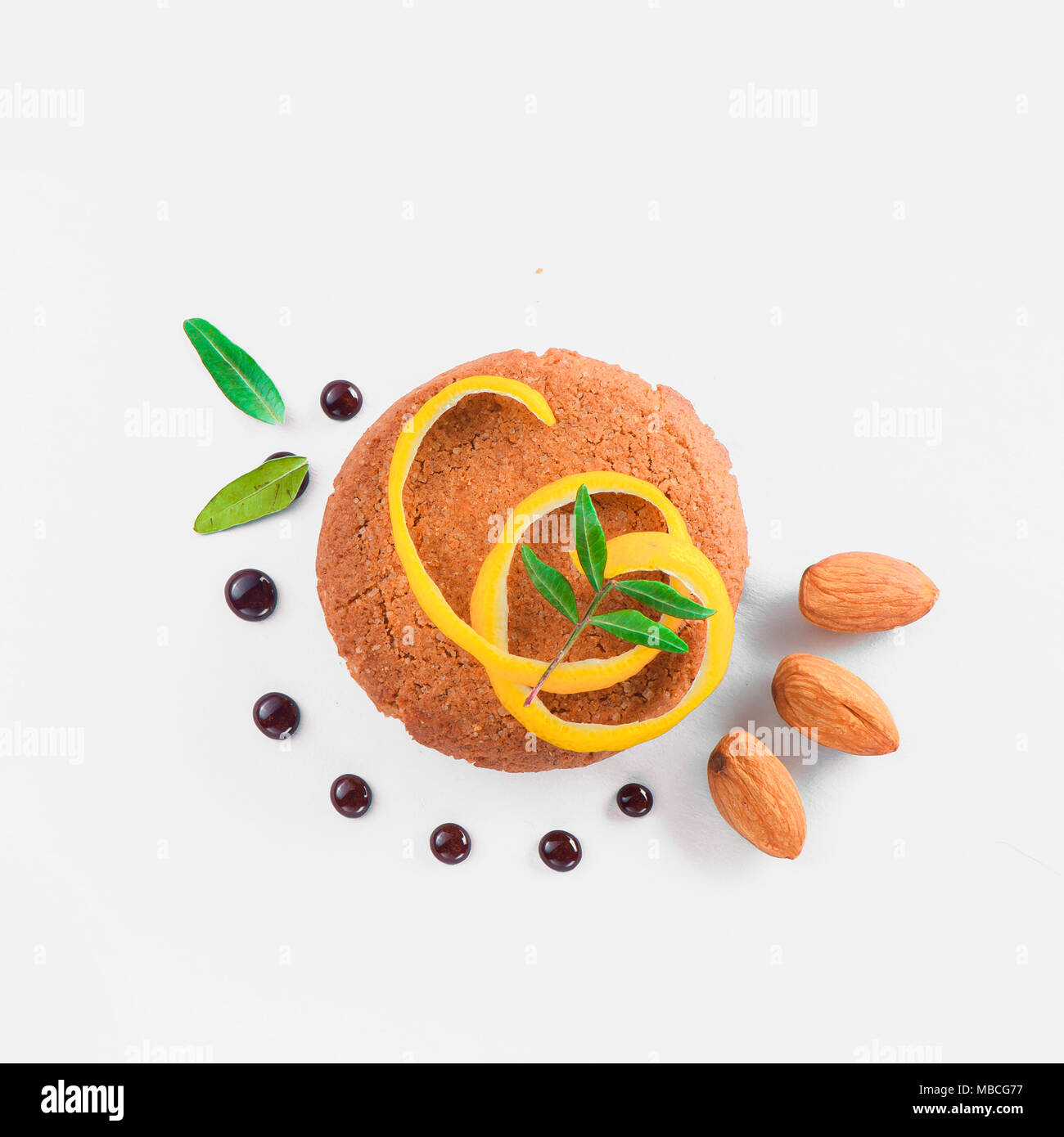 Cookie decorated with lemon zest, almond and green leaves on a white ...