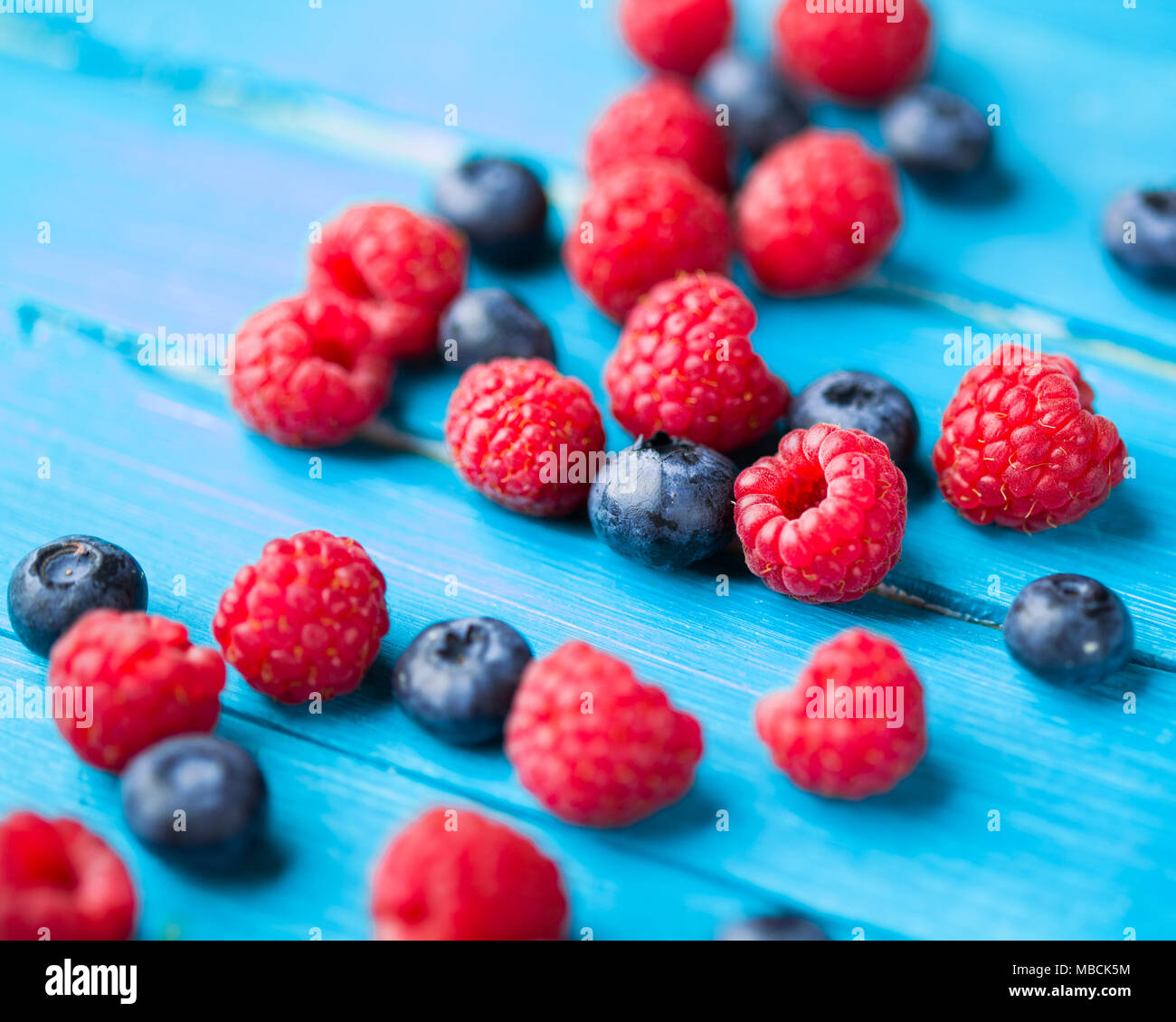 Blueberries and raspberries on blue wooden table Stock Photo - Alamy