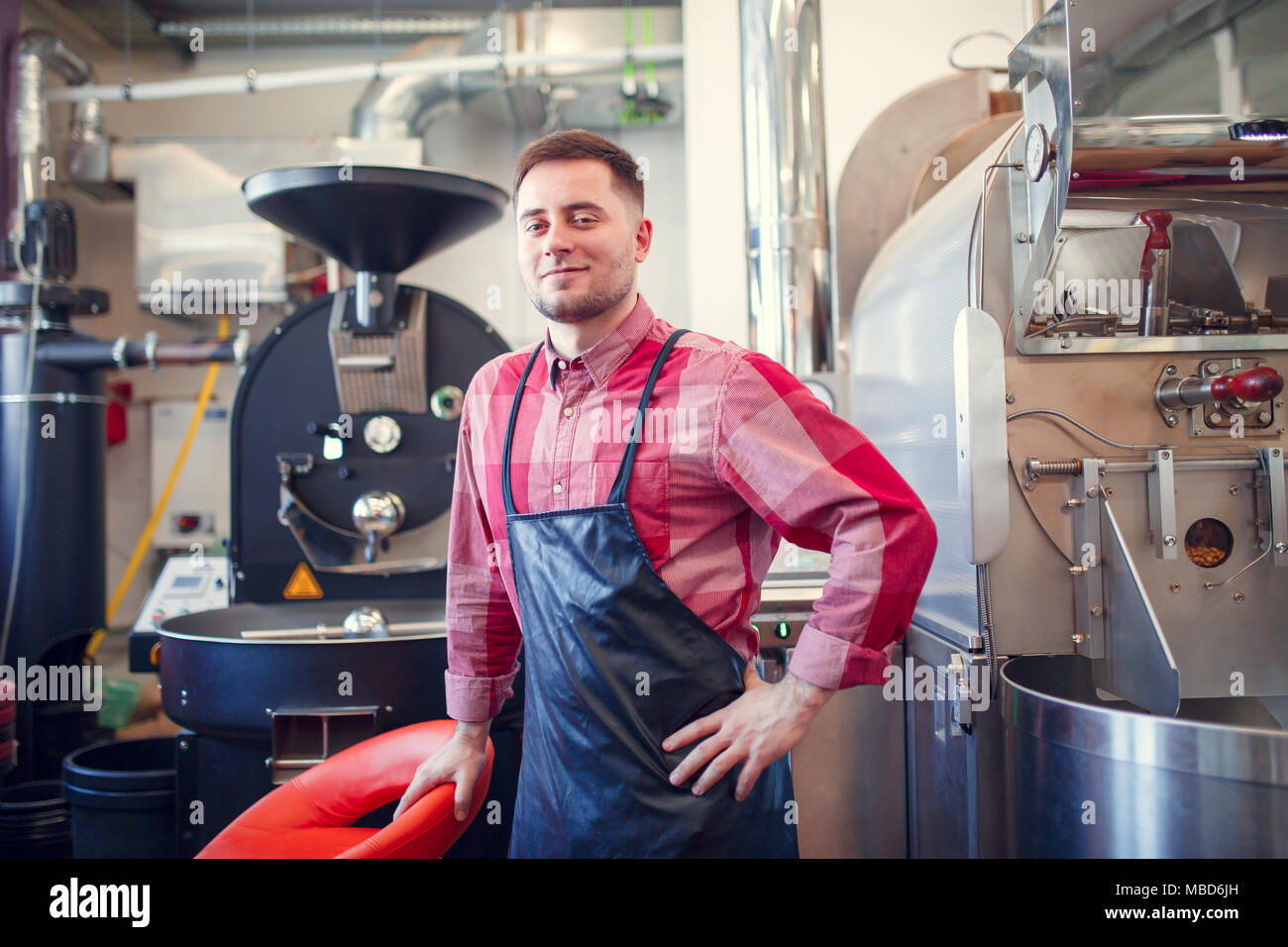 Photo of happy man in apron on background of industrial coffee grinder ...
