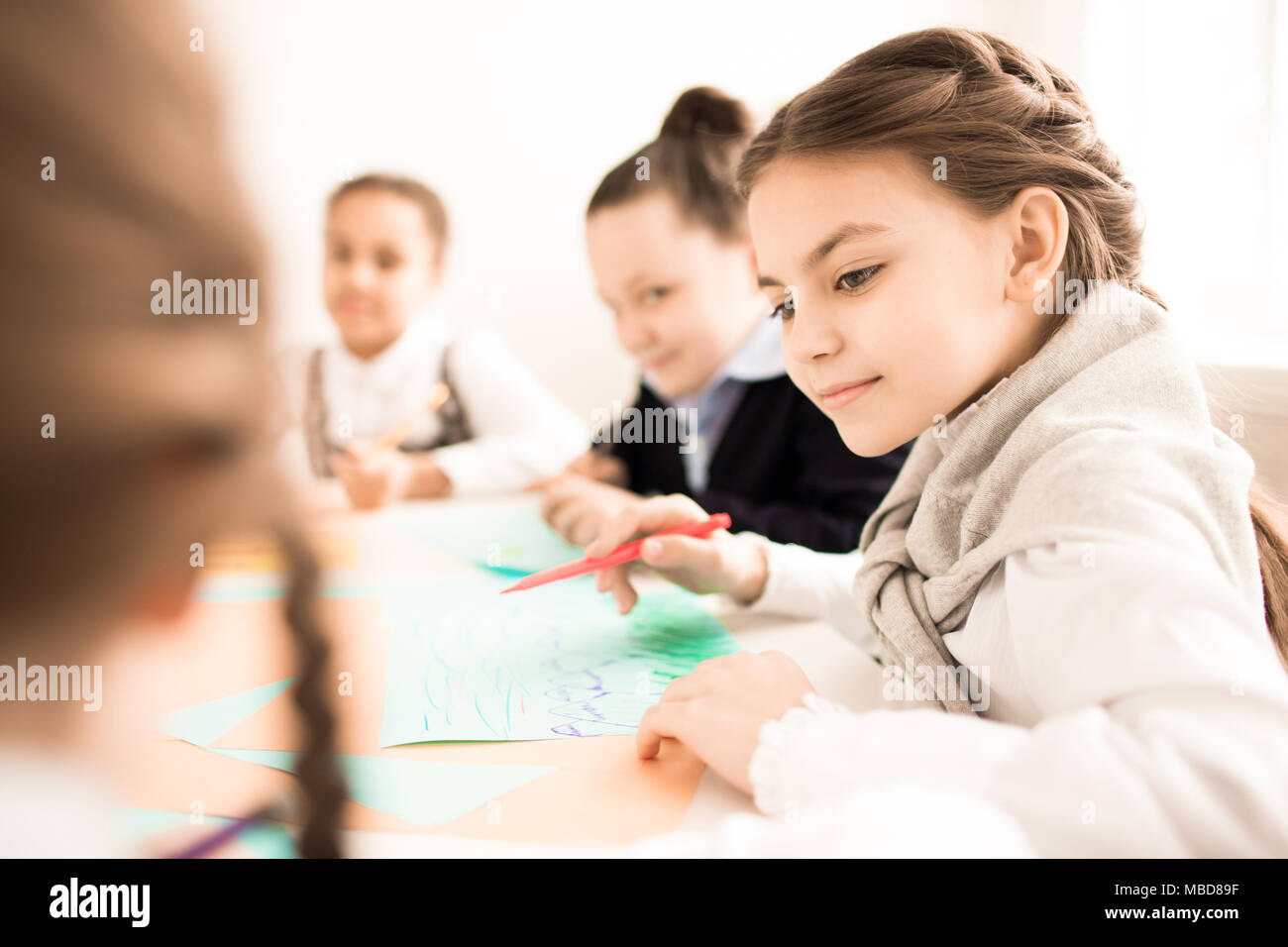 Little girl drawing a picture together with her classmates at the table ...
