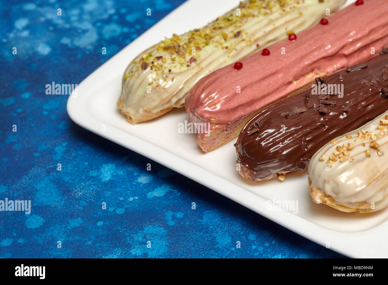 Four colorful eclair cakes with cream on blue background, copyspace ...