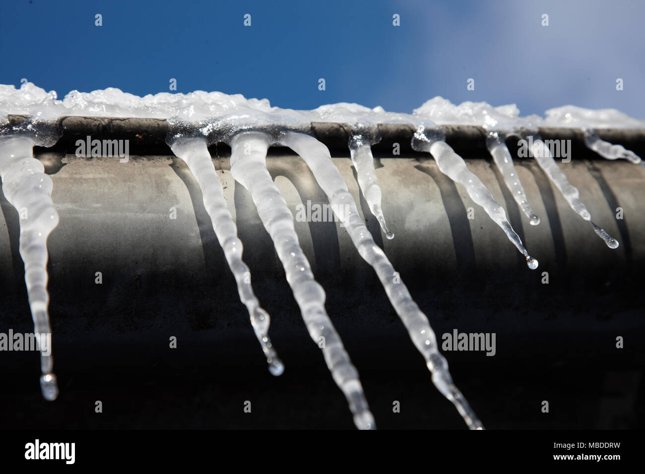 Icicle in the eaves spout with a blue sky background Stock Photo - Alamy