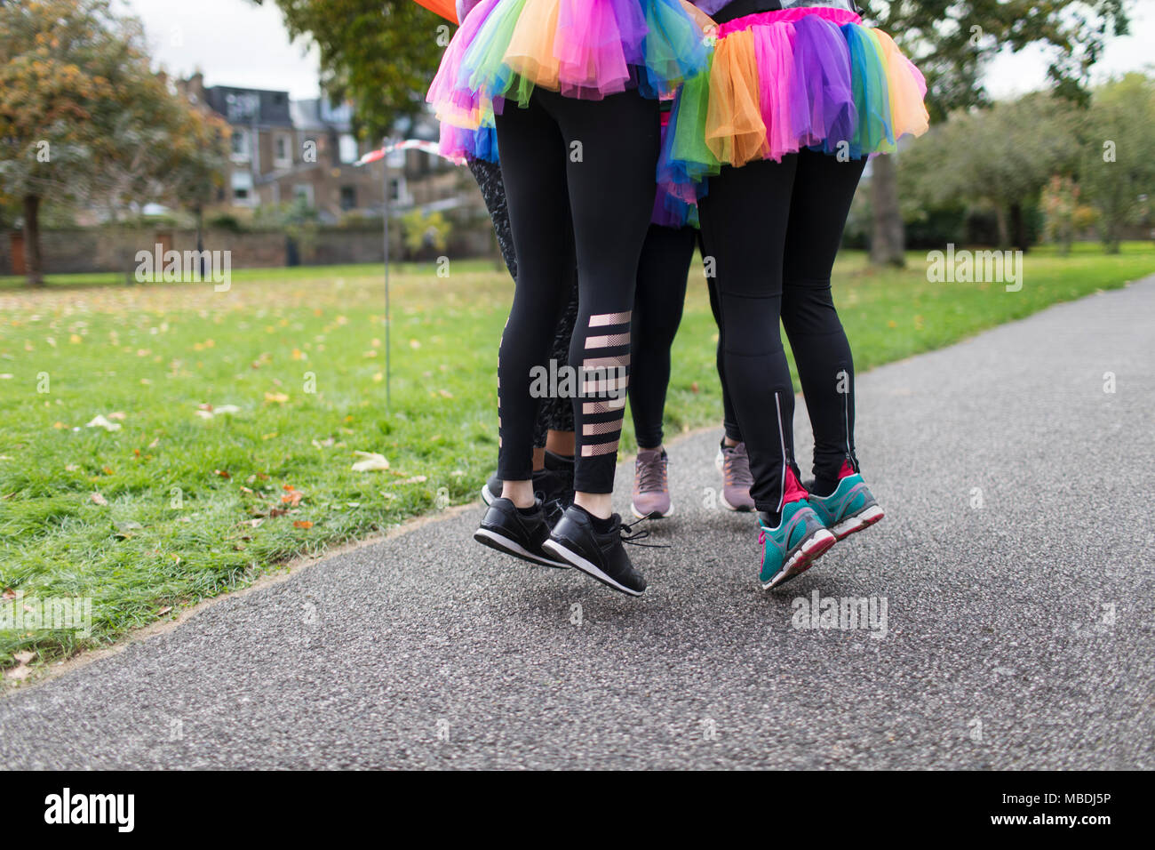 Enthusiastic female runners in tutus jumping on park path Stock Photo ...
