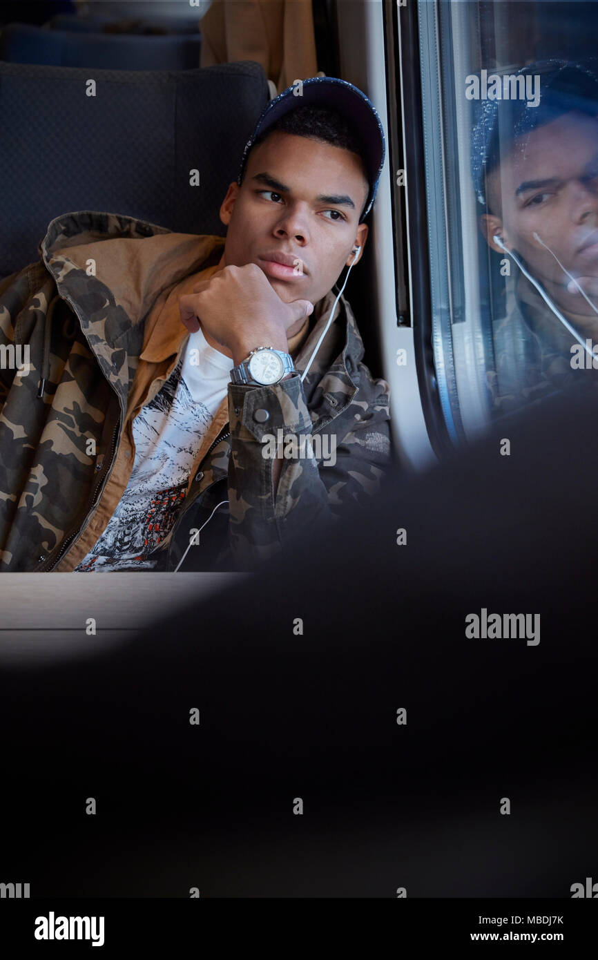 Serious, thoughtful young man looking out window on passenger train ...