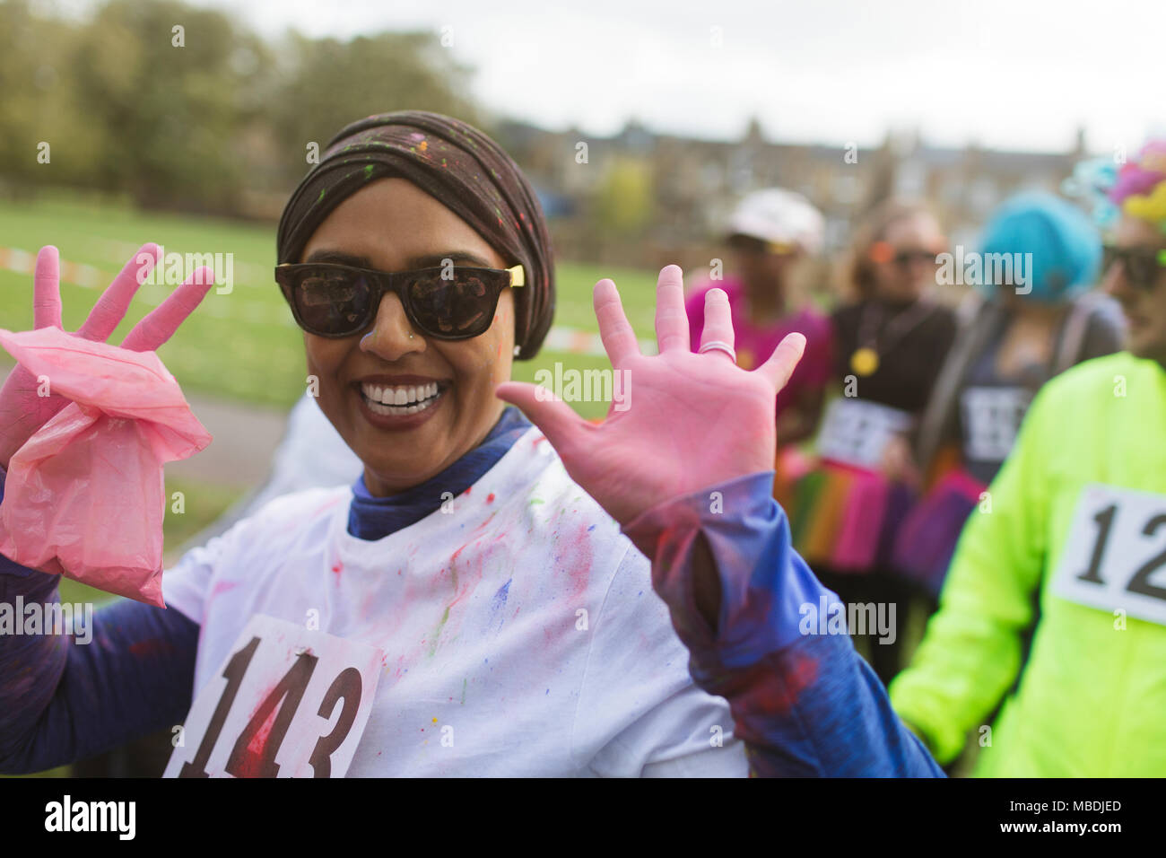 Portrait enthusiastic female runner with pink holi powder hands at ...