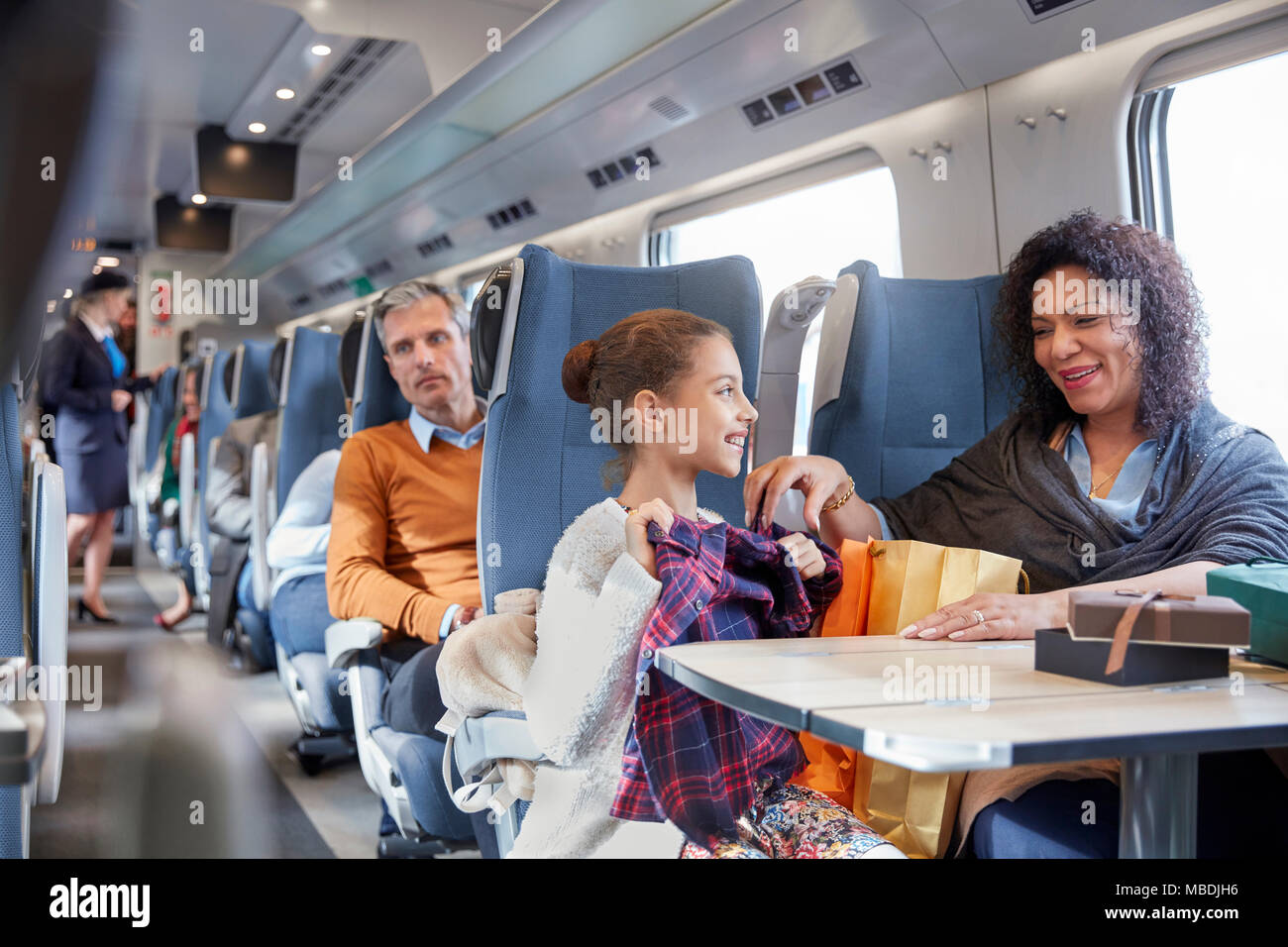 Mother And Daughter Looking At New Clothes On Passenger Train Stock