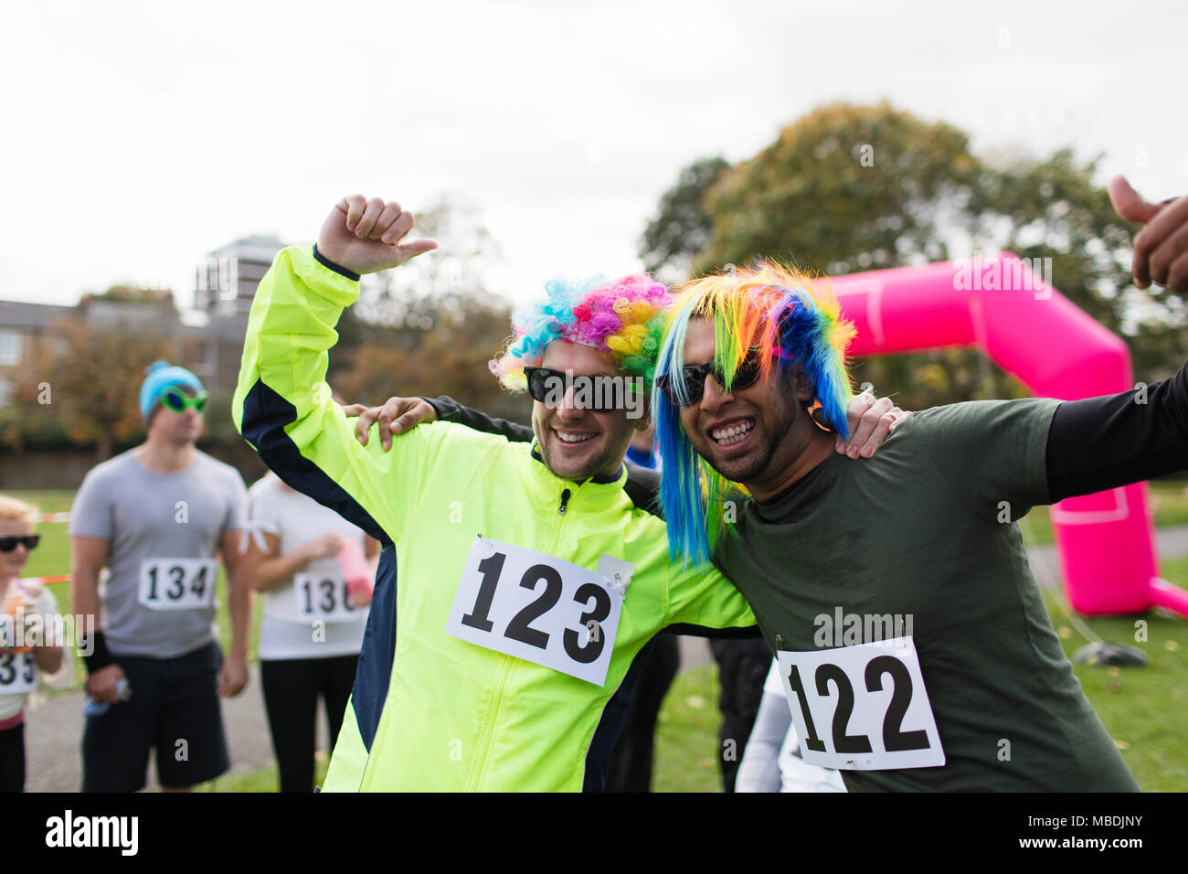 Portrait playful male runners wearing wigs and cheering at charity run ...