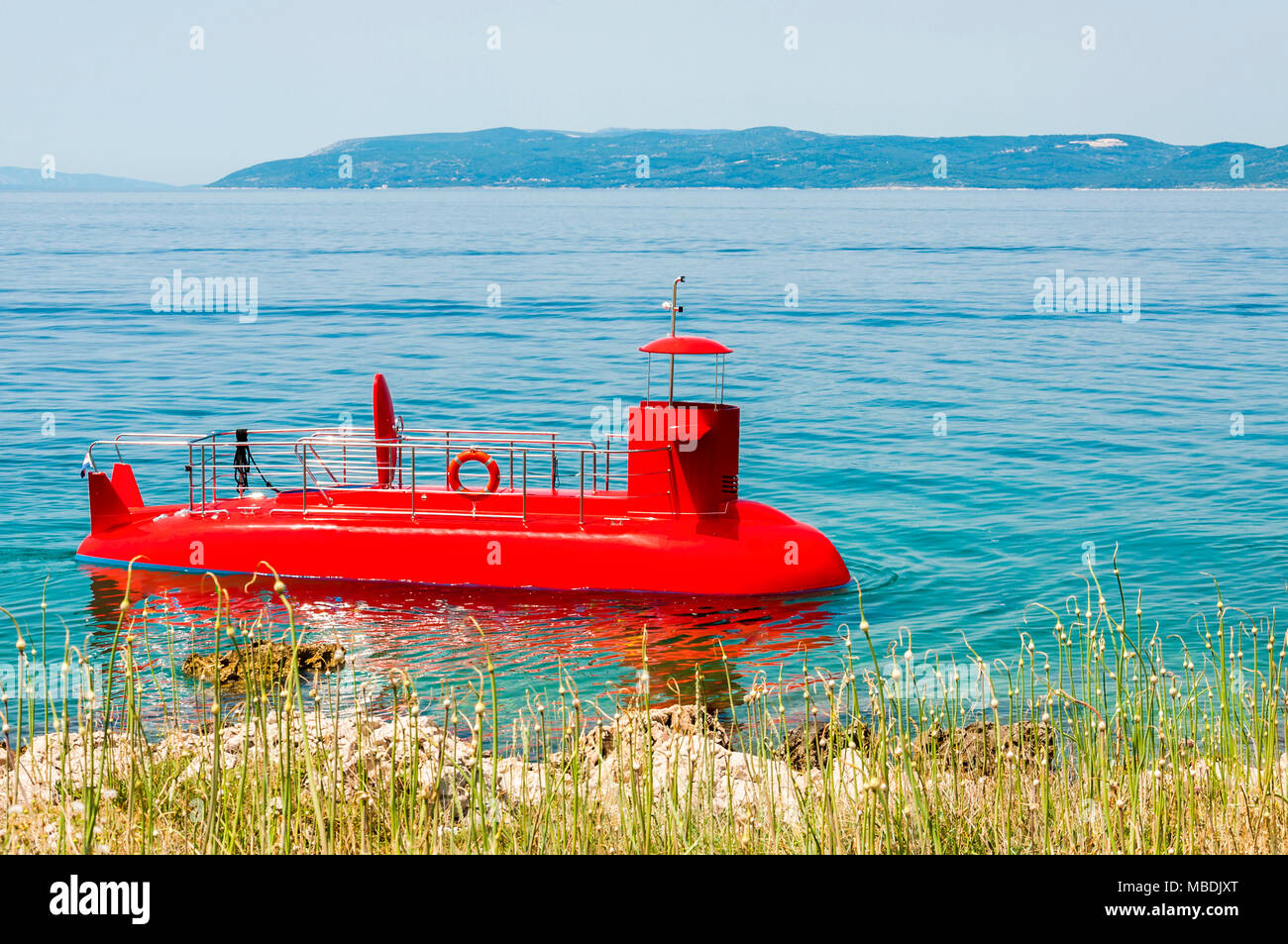 Vibrant red sea ship floating near rocky coastline Stock Photo - Alamy
