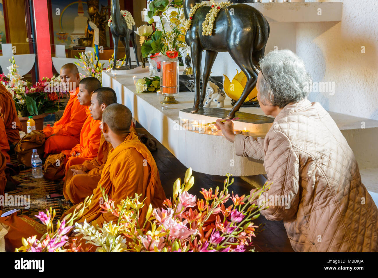 An old woman lights incense sticks while buddhist monks seated on the ...