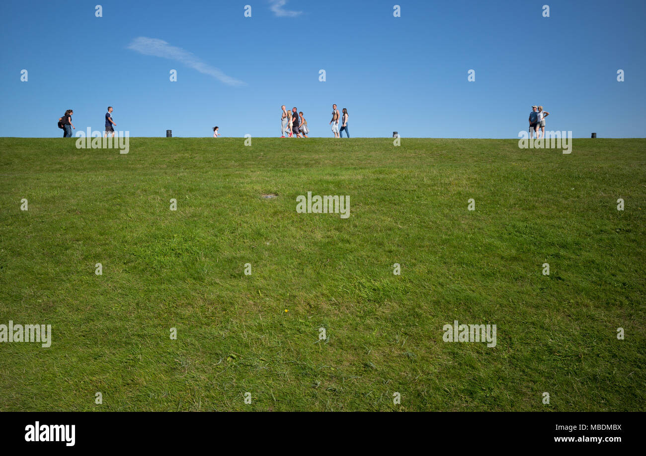 Visitors walking along top of grass covered embankment forming part of ...