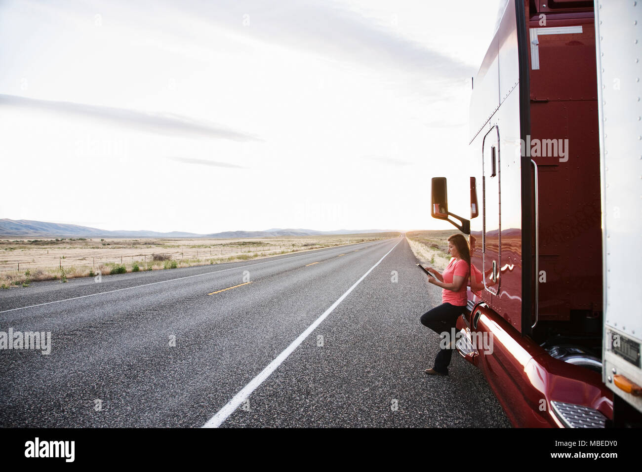 Female truck driver standing next to the cab of her truck near the ...