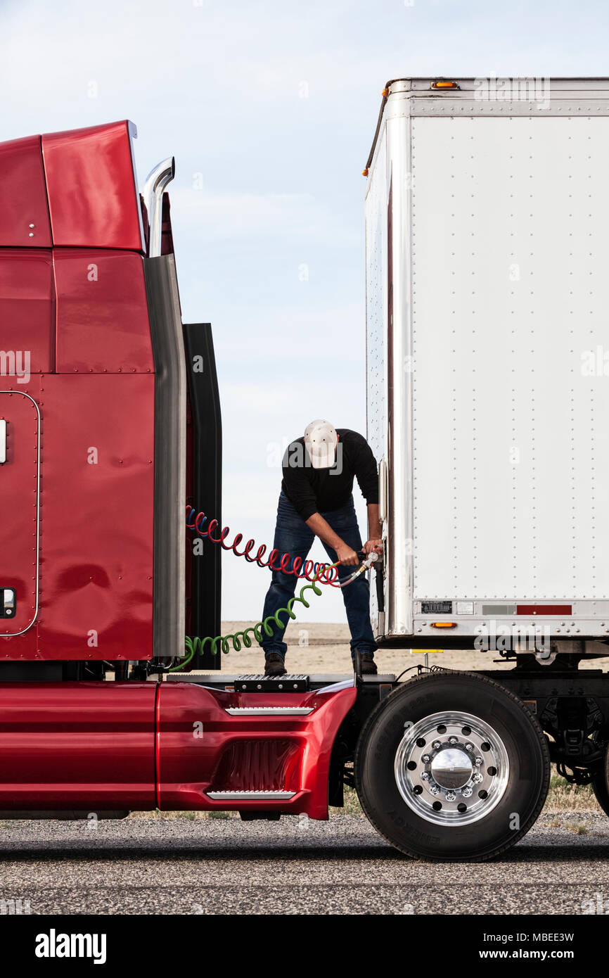 View of a driver connectiing the power cables to trailer of a ...