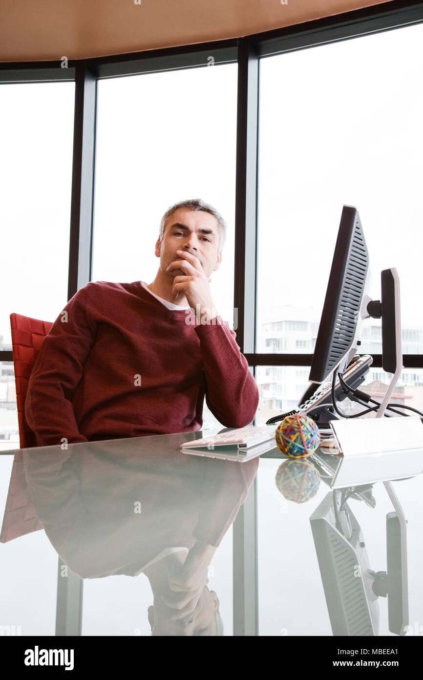 Casually dressed caucasian businessman relaxed at his reflective desk ...
