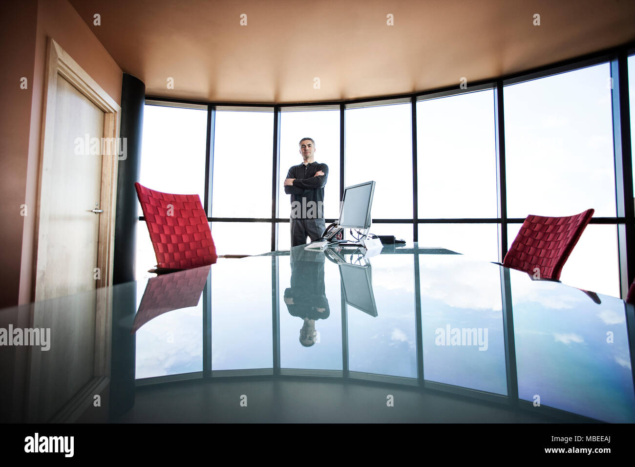 Casually dressed caucasian businessman relaxed at his reflective desk ...