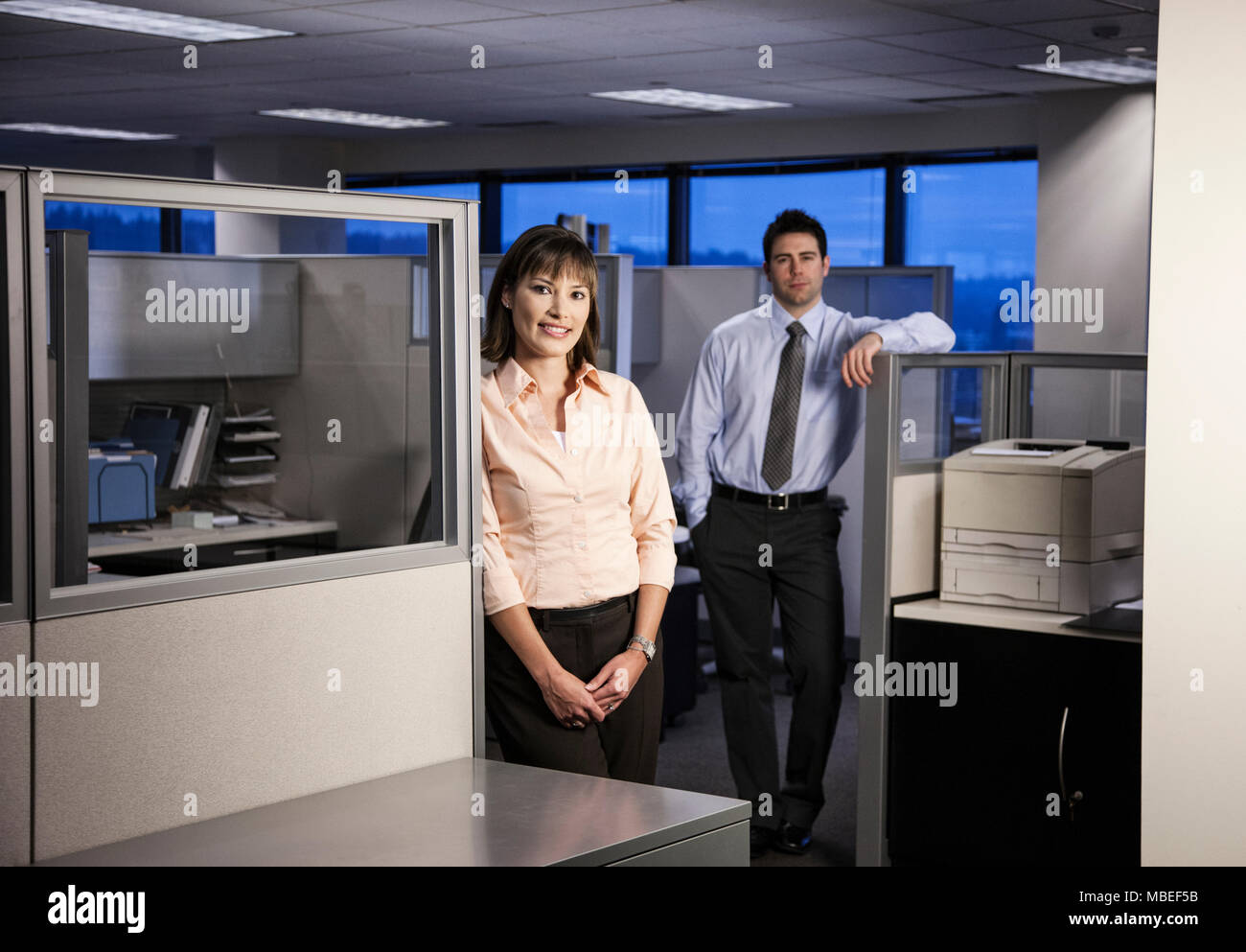 Two young business people working into the evening in a cubicle office ...