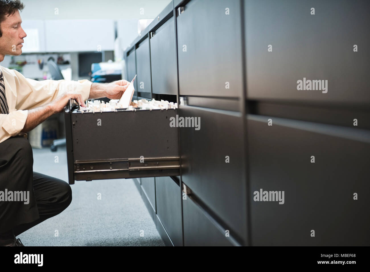 Caucasian businessman pulling files from a traditional file cabinet ...