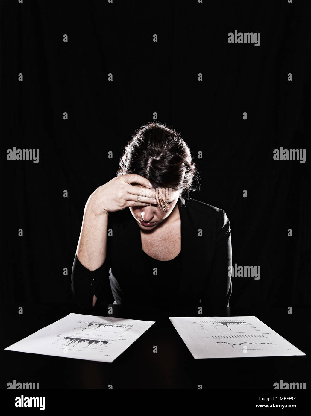 A woman seated with her hand on her forehead, reading documents. Studio ...