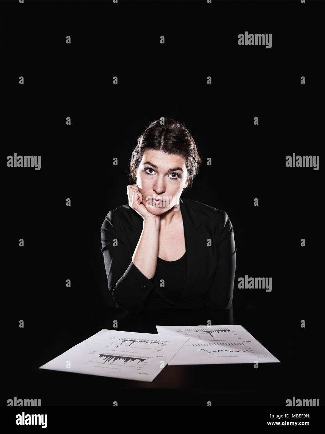 Studio portrait, a woman sitting with paperwork spread out and her hand ...