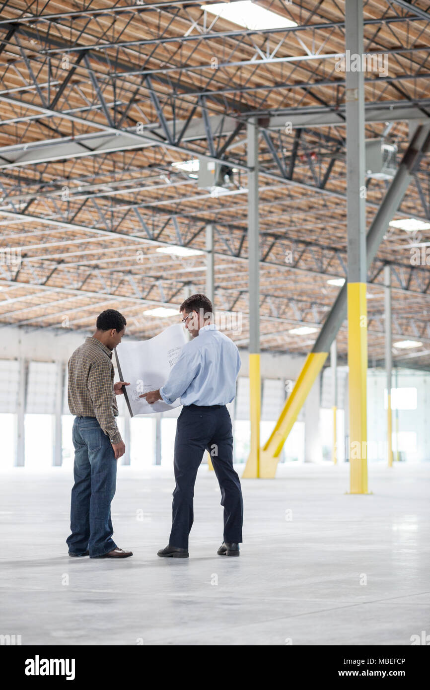 Back man owner of new warehouse and caucasian man architect going over ...