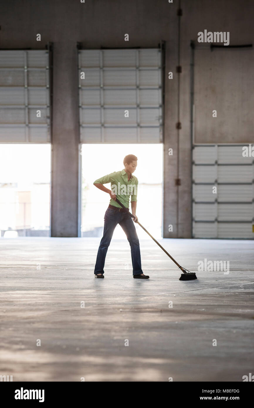 Black woman sweeping up in an empty warehouse space Stock Photo - Alamy