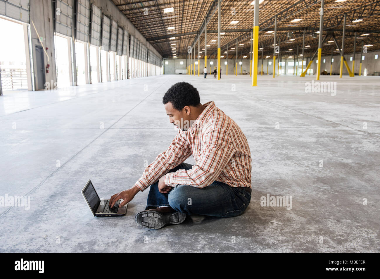 Black man working on lap top computer in front of loading dock doors in ...