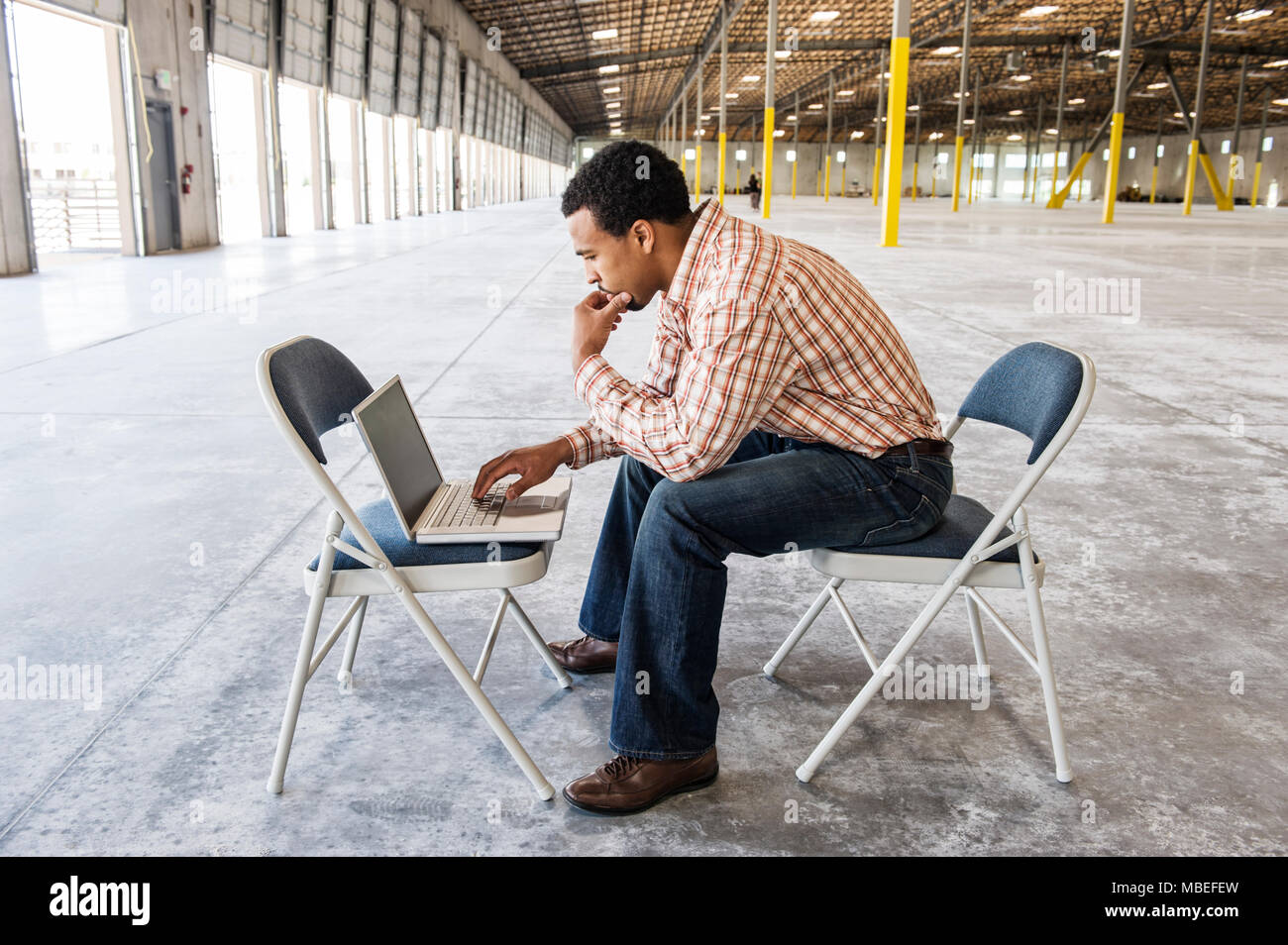 Black man working on lap top computer in front of loading dock doors in ...