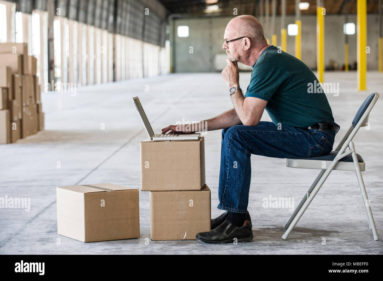 Caucasian man using boxes as desk and working on lap top computer in ...