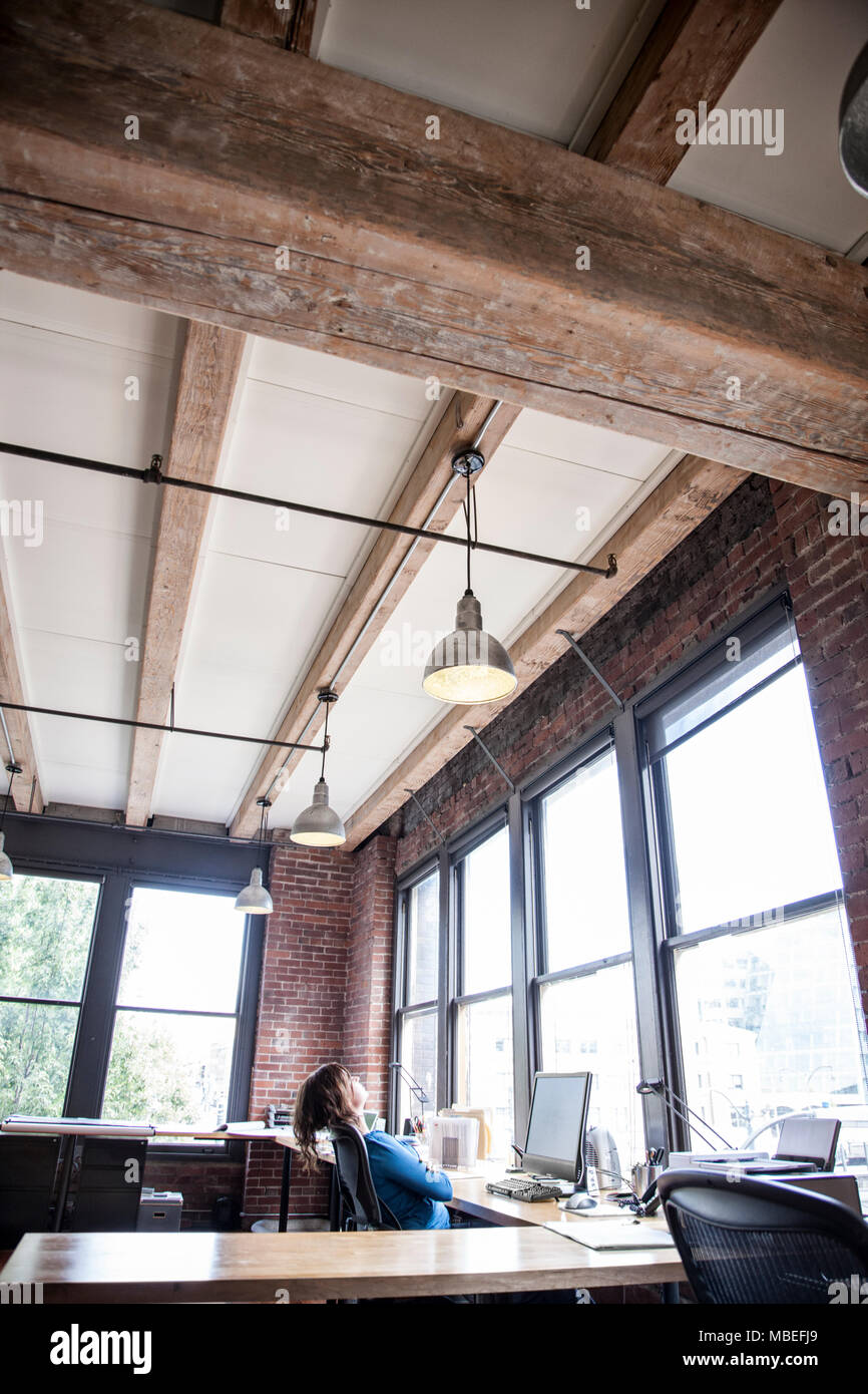 Caucasian woman at office workstation near a large bank of windows ...