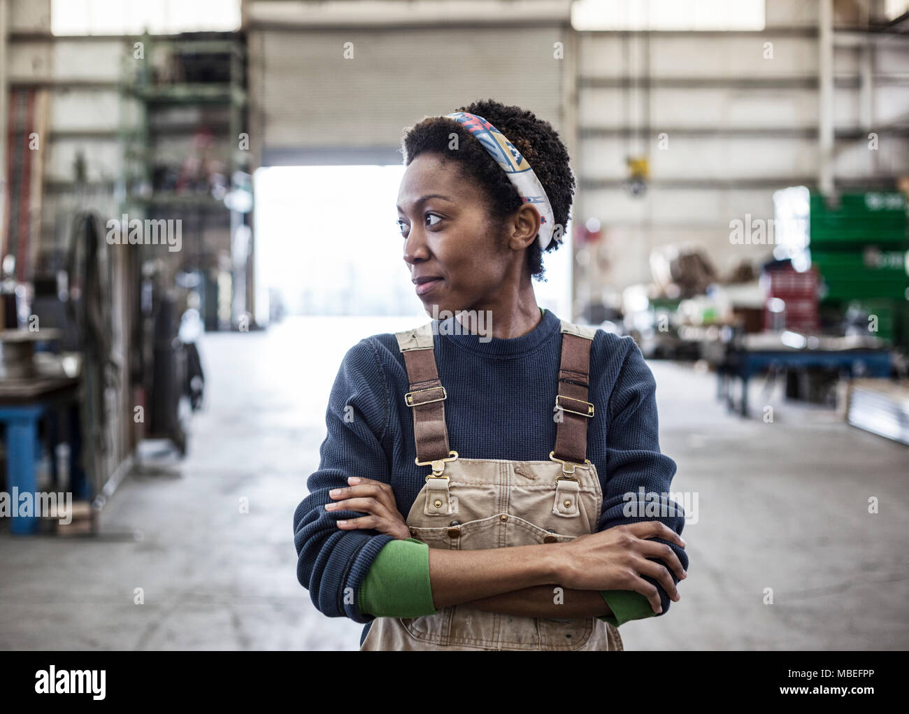 Black woman factory worker wearing coveralls in a large sheet metal ...