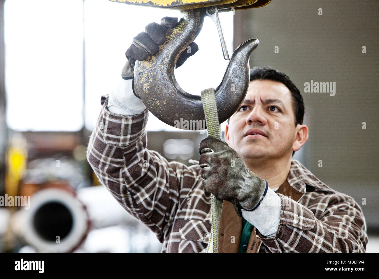 Hispanic man factory worker attaching a strap to the hook of a heavy ...