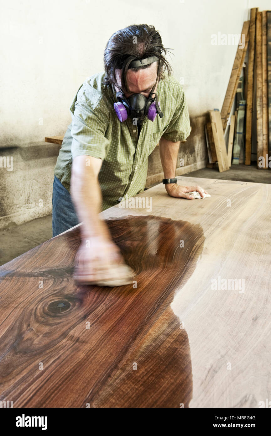 Caucasian man factory worker applying finish to a recylced wood table ...
