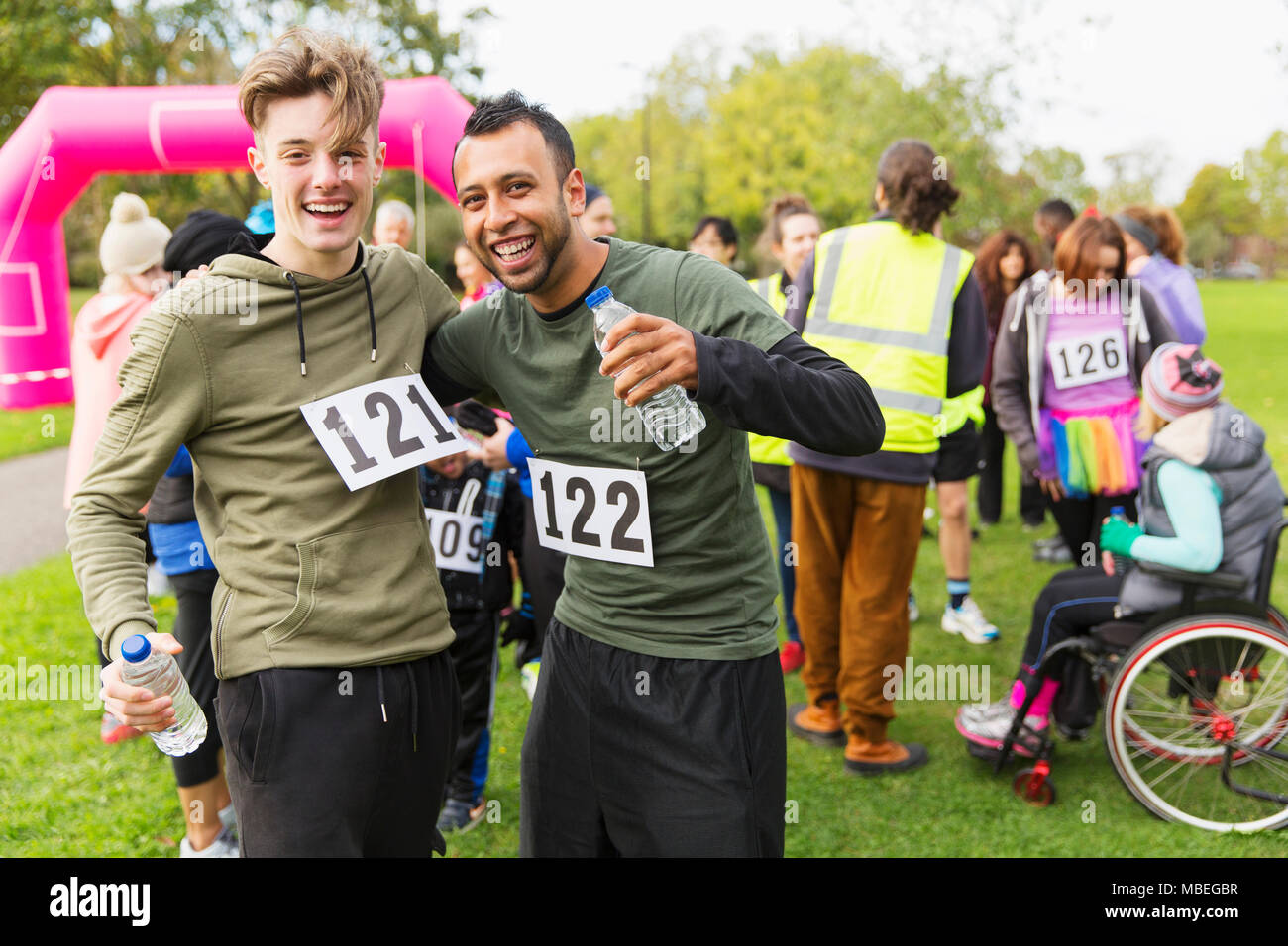 Portrait enthusiastic male runner friends with water hugging at charity ...