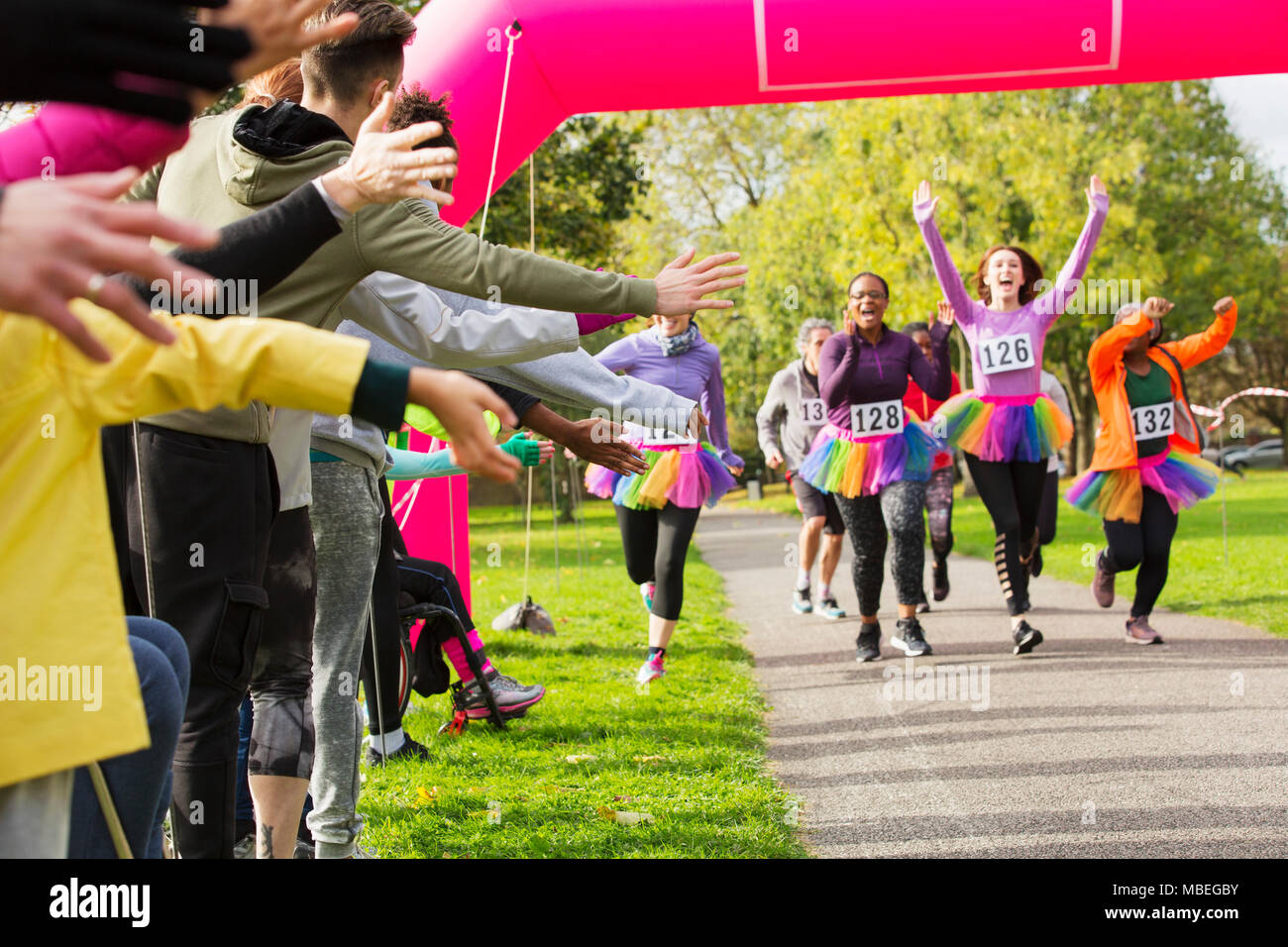 Enthusiastic female runners in tutus nearing finish line at charity run ...