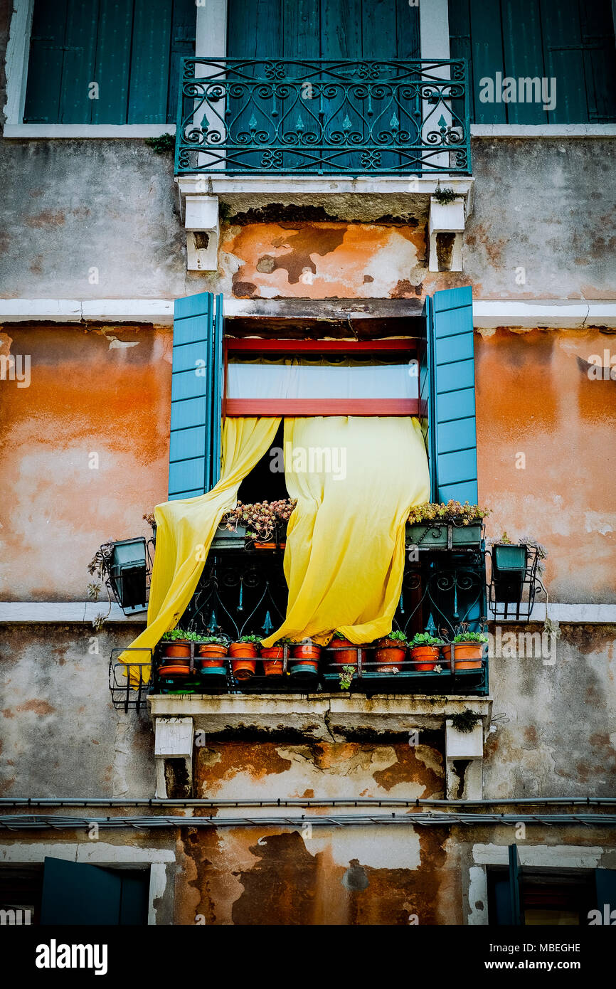 A yellow curtain draped and blowing in the wind out of an old window in ...