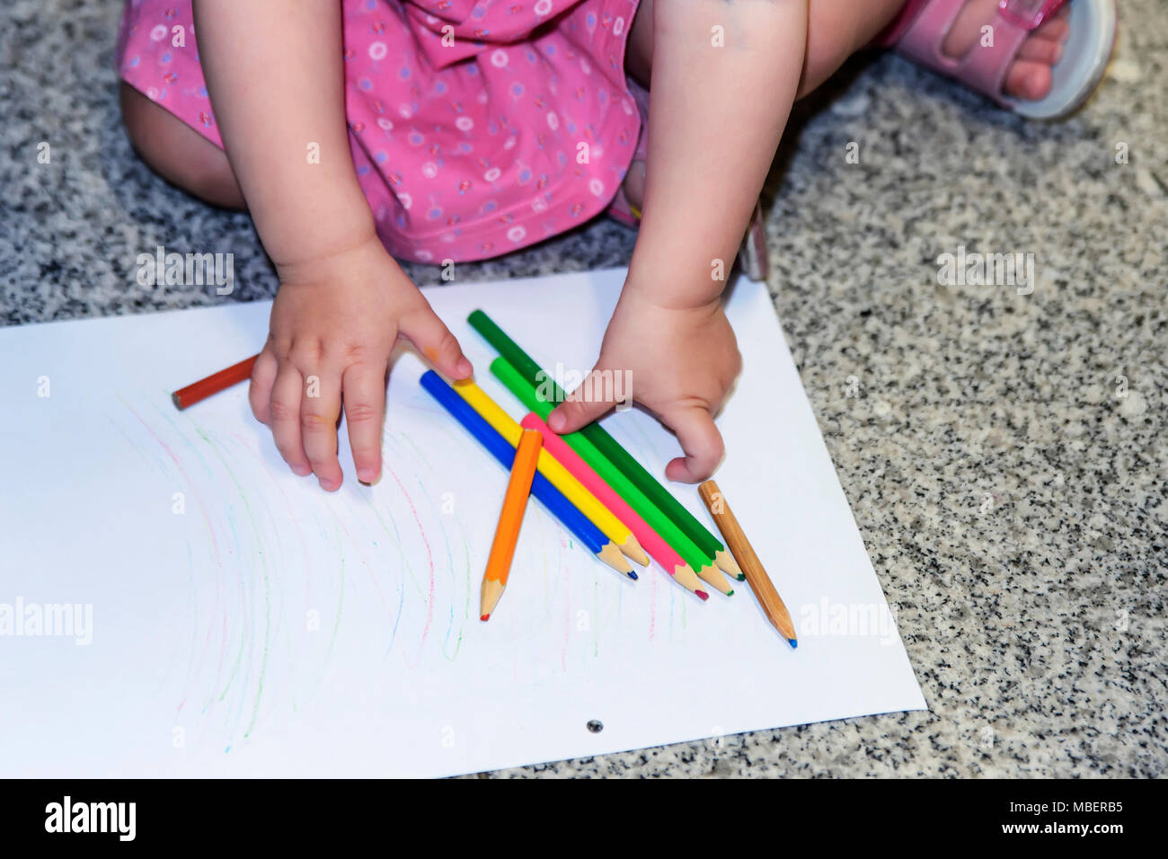hands of a small child reach for the colored pencils lying on white ...