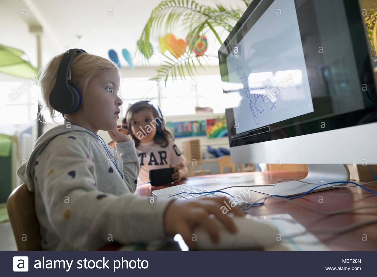 Preschool girl student wearing headphones, using computer in classroom ...