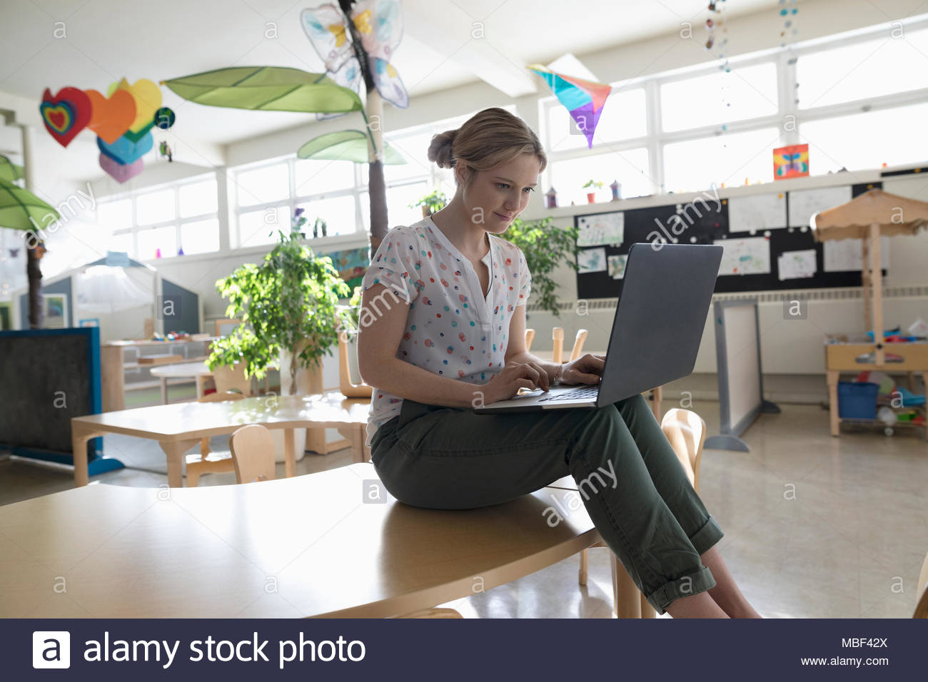 Preschool teacher using laptop in classroom Stock Photo - Alamy