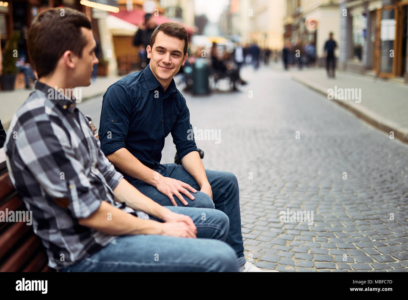 Two man sit on bench and talk on the street Stock Photo - Alamy