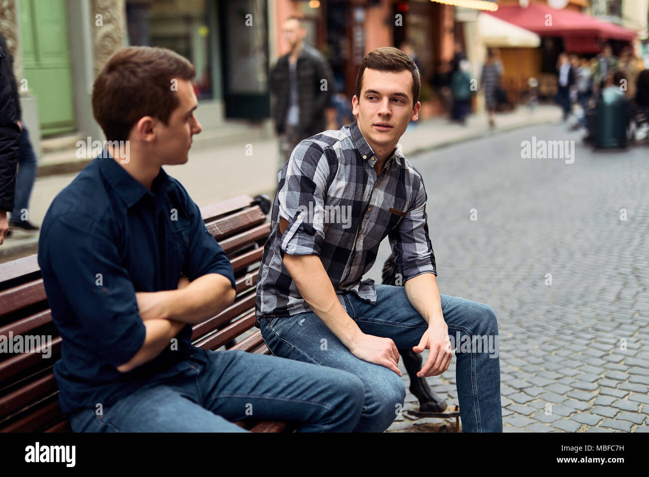 Two man sit on bench and talk on the street Stock Photo - Alamy