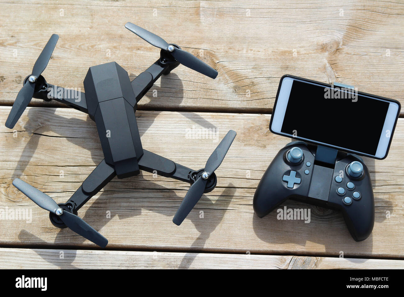 Black Drone quadcopter with a remote control and phone on wood table ...