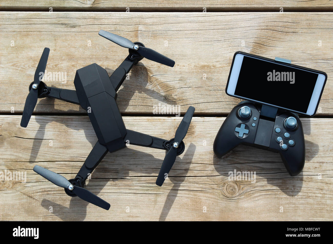Black Drone quadcopter with a remote control and phone on wood table ...