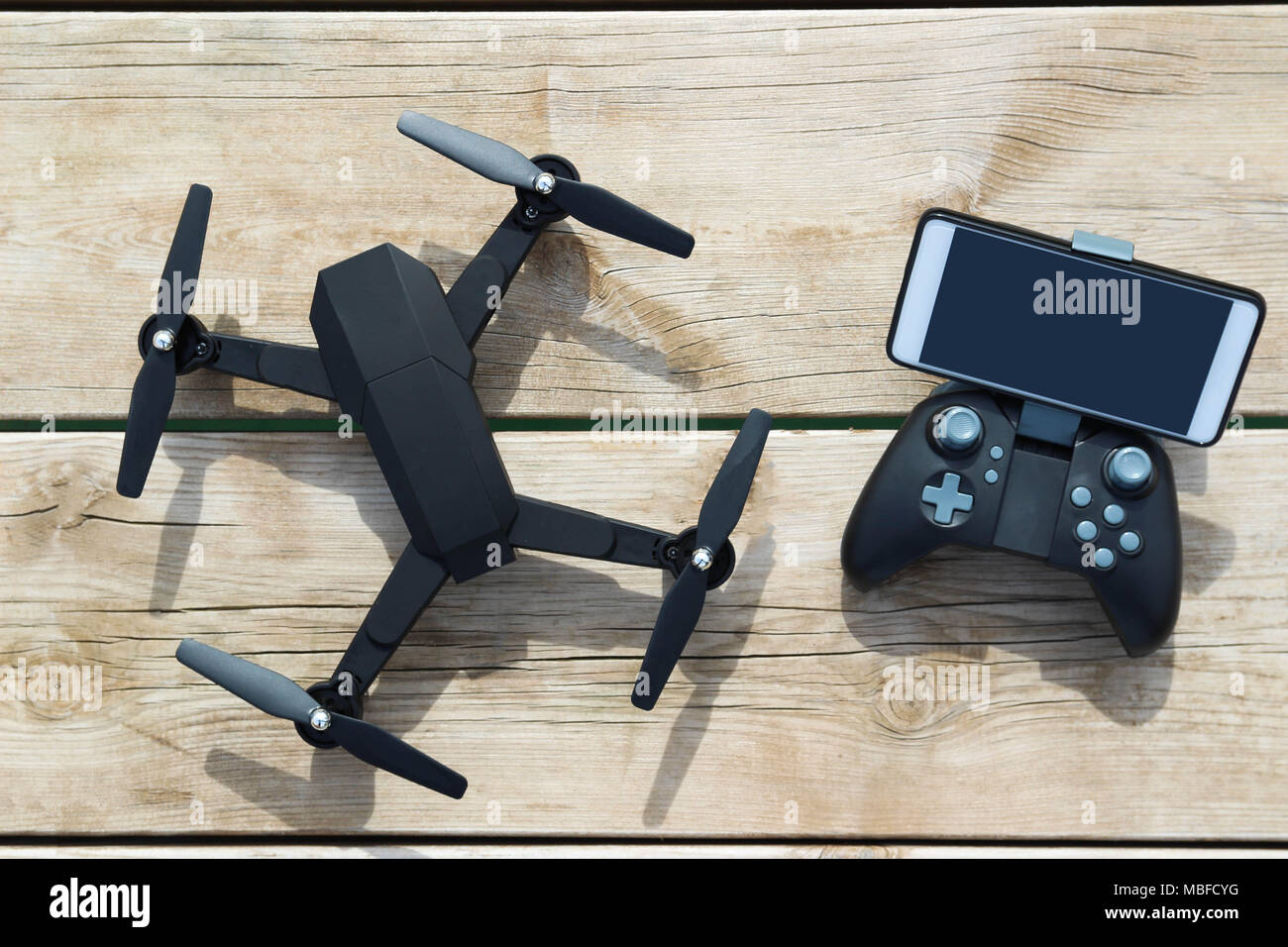 Black Drone quadcopter with a remote control and phone on wood table ...